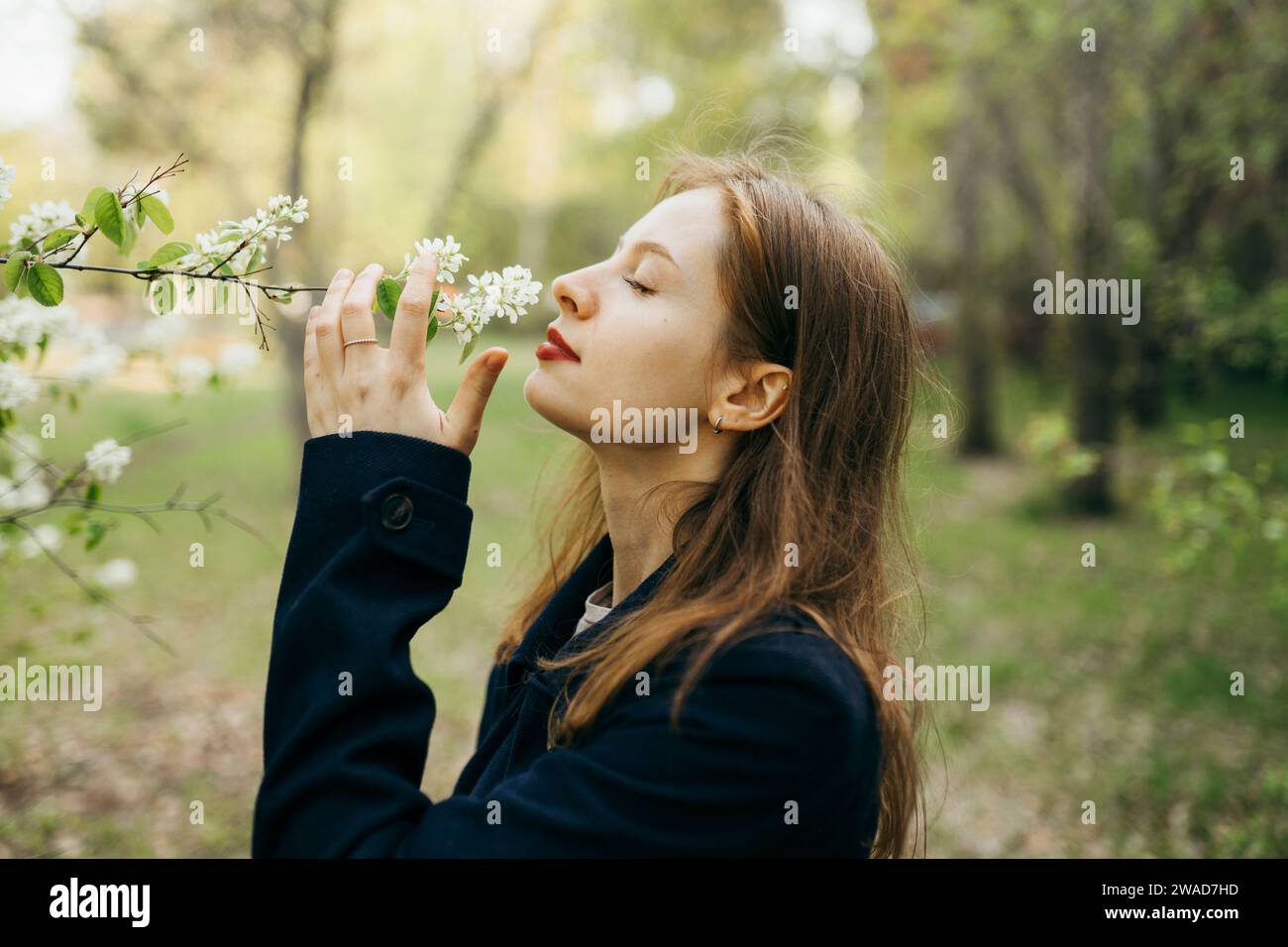 Beautiful woman smelling flower in orchard Stock Photo - Alamy