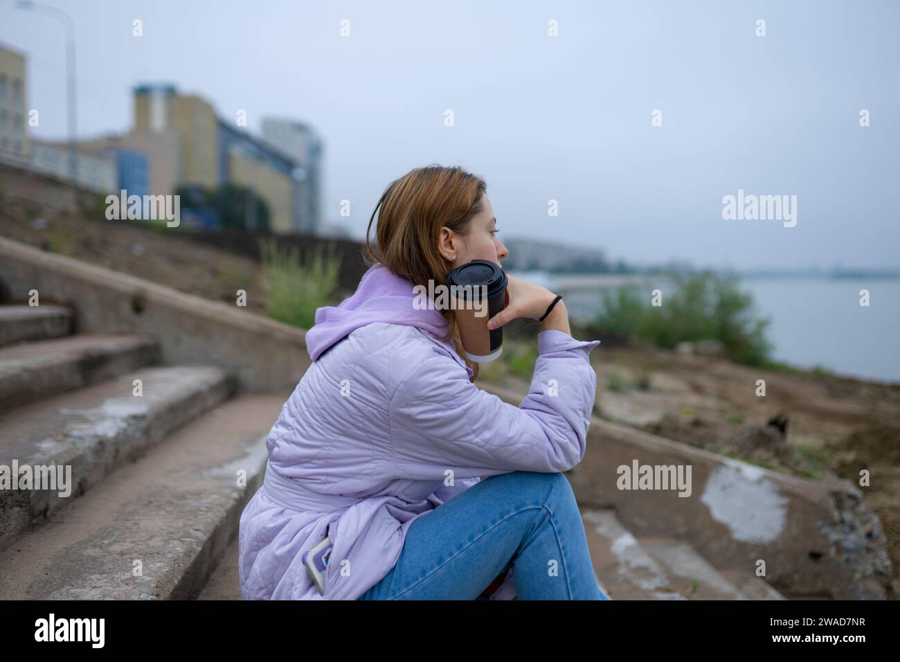 Thoughtful woman sitting on steps and looking at river Stock Photo - Alamy
