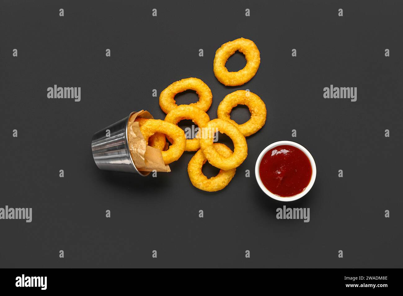 Metal bucket with fried breaded onion rings and ketchup on black ...