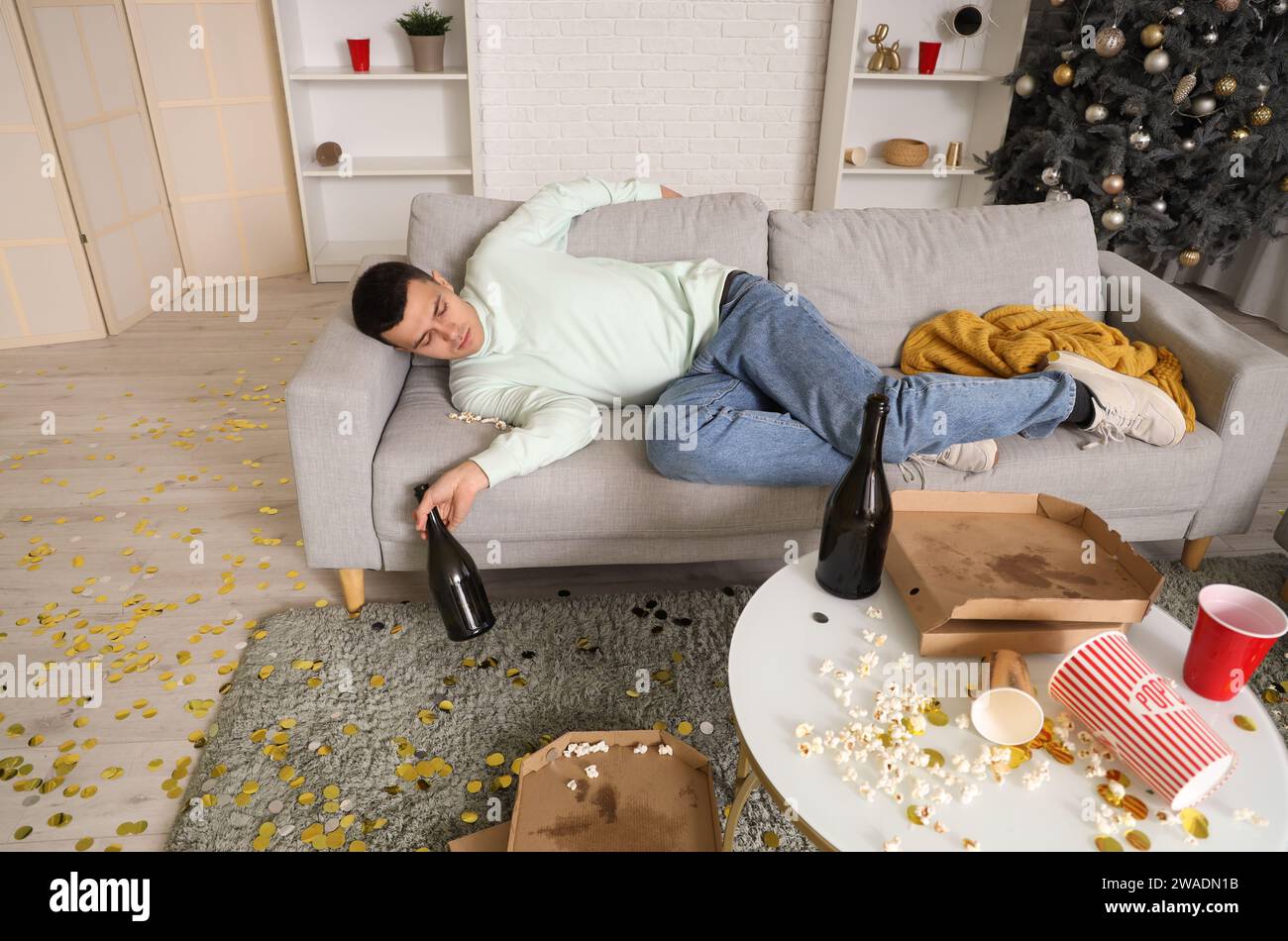 Drunk young man with champagne sleeping on sofa after New Year party at ...