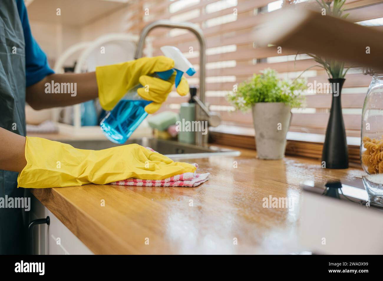Woman in uniform smiling cleaning kitchen desk with disinfectant spray ...
