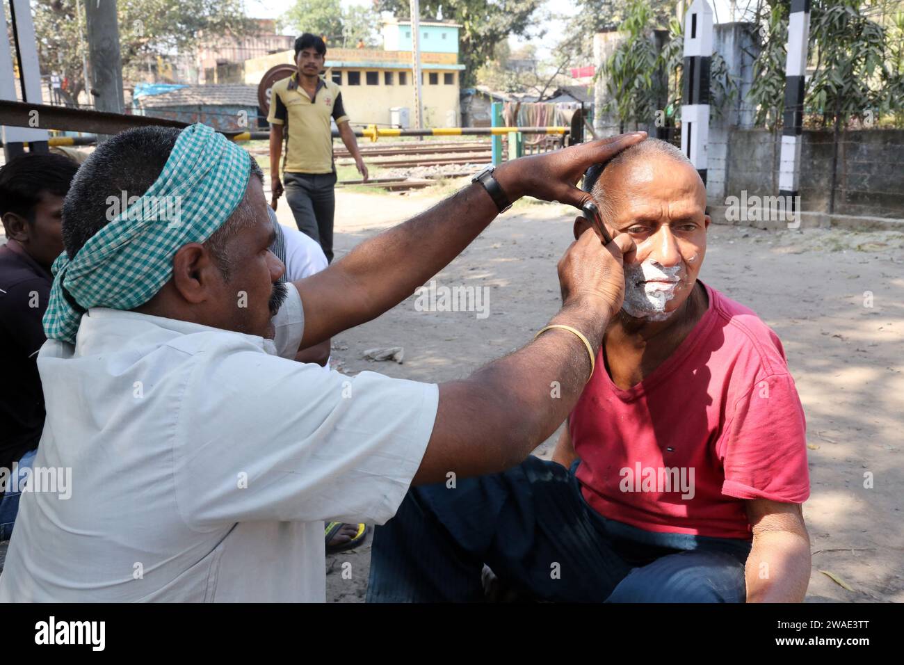 Street barber shaving a man using an open razor blade on a street in ...