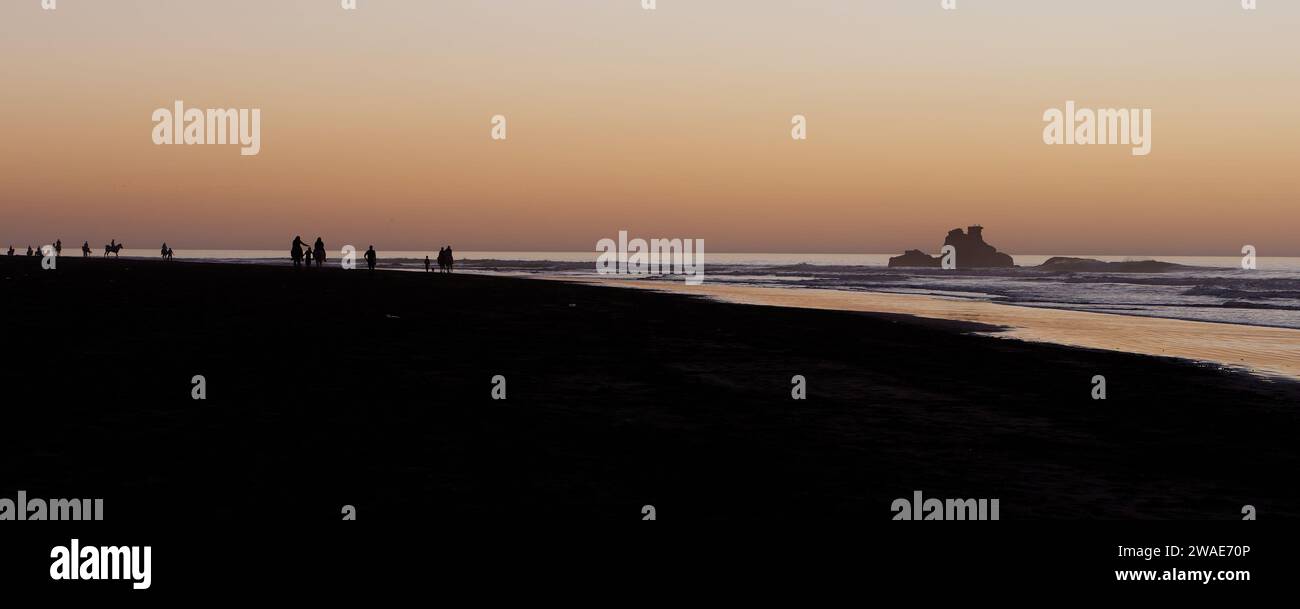 Beach horse riders at sunset in silhouette with a rock outcrop as the ...