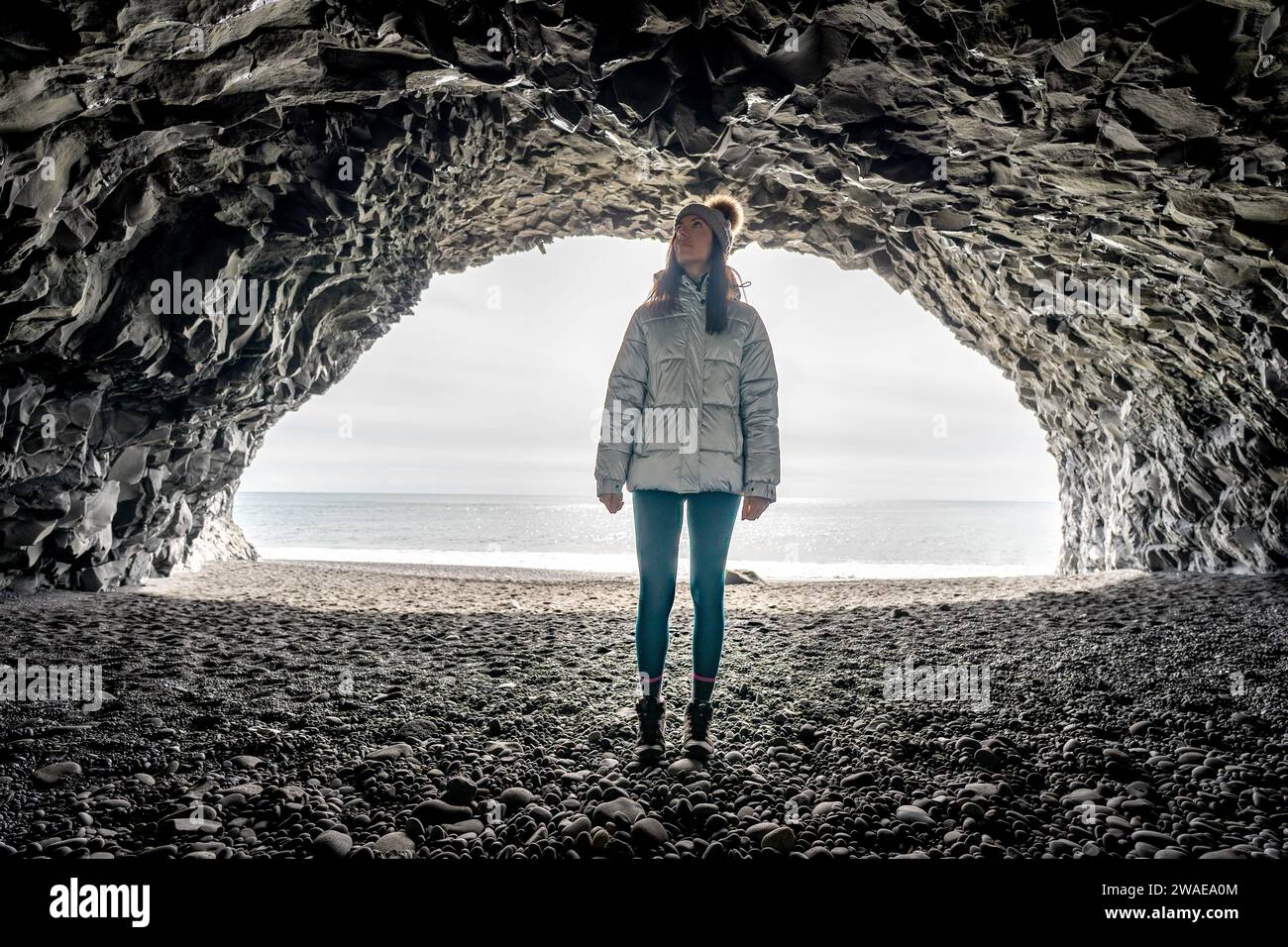 A young woman stands in front of a dark cave with vibrant blue and ...