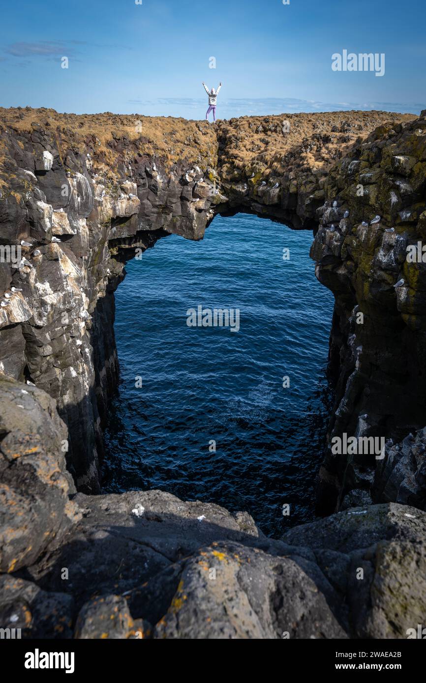 A man stands on the edge of a stone arch, overlooking the ocean below ...