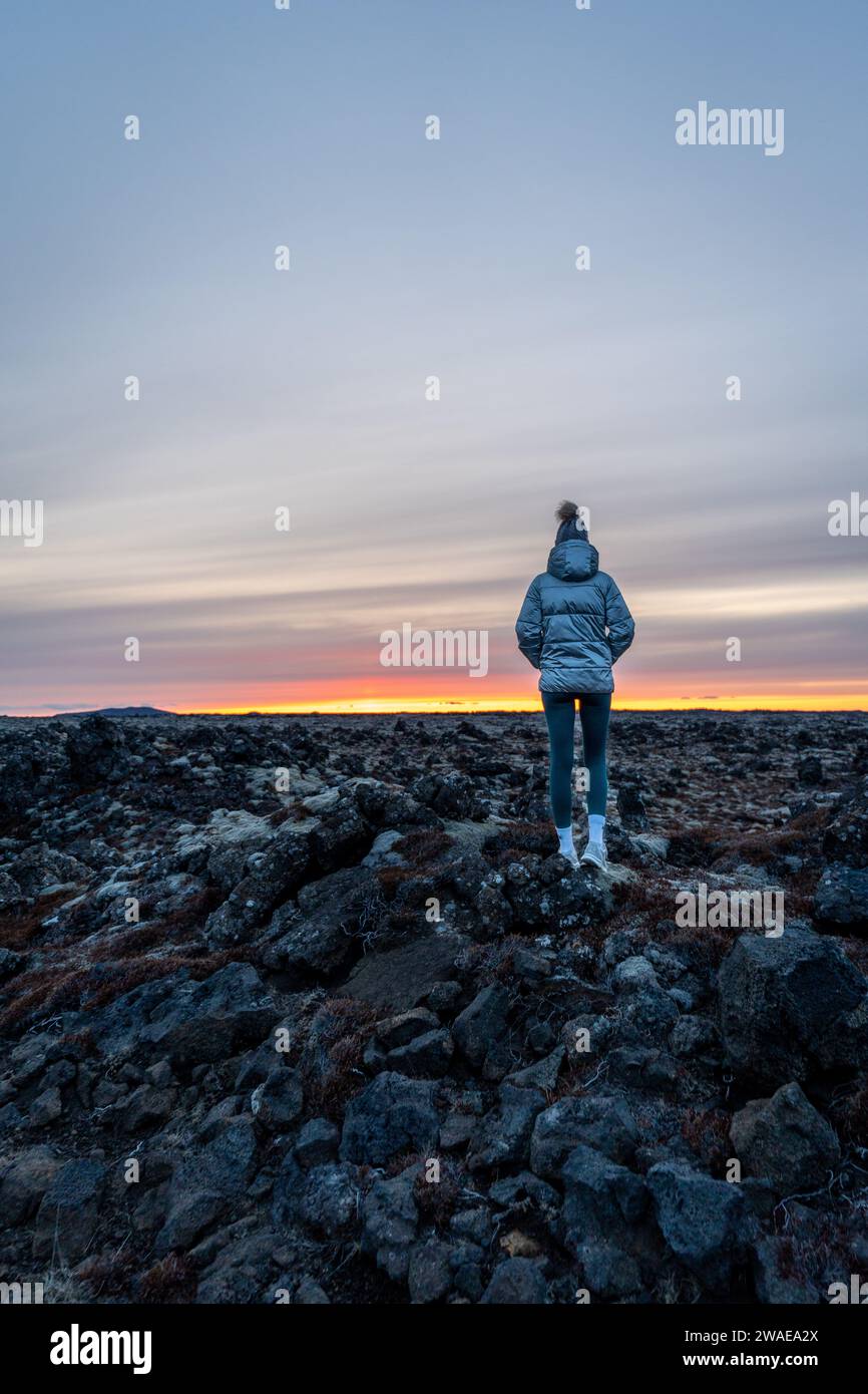 A silhouetted figure stands on a rocky outcrop in a grassy landscape ...