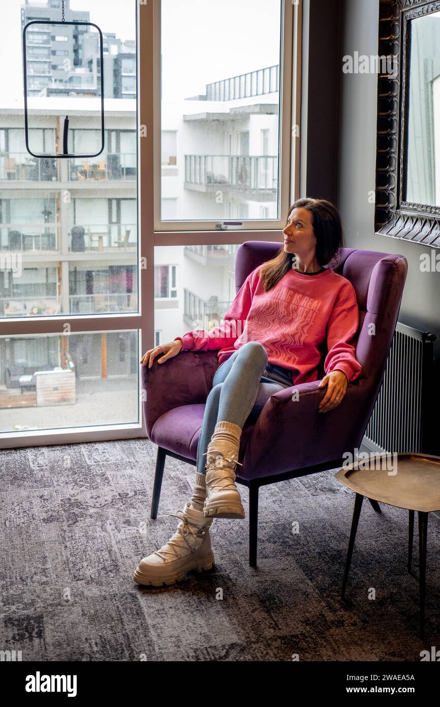 A young female is sitting in a vibrant purple armchair, her legs ...