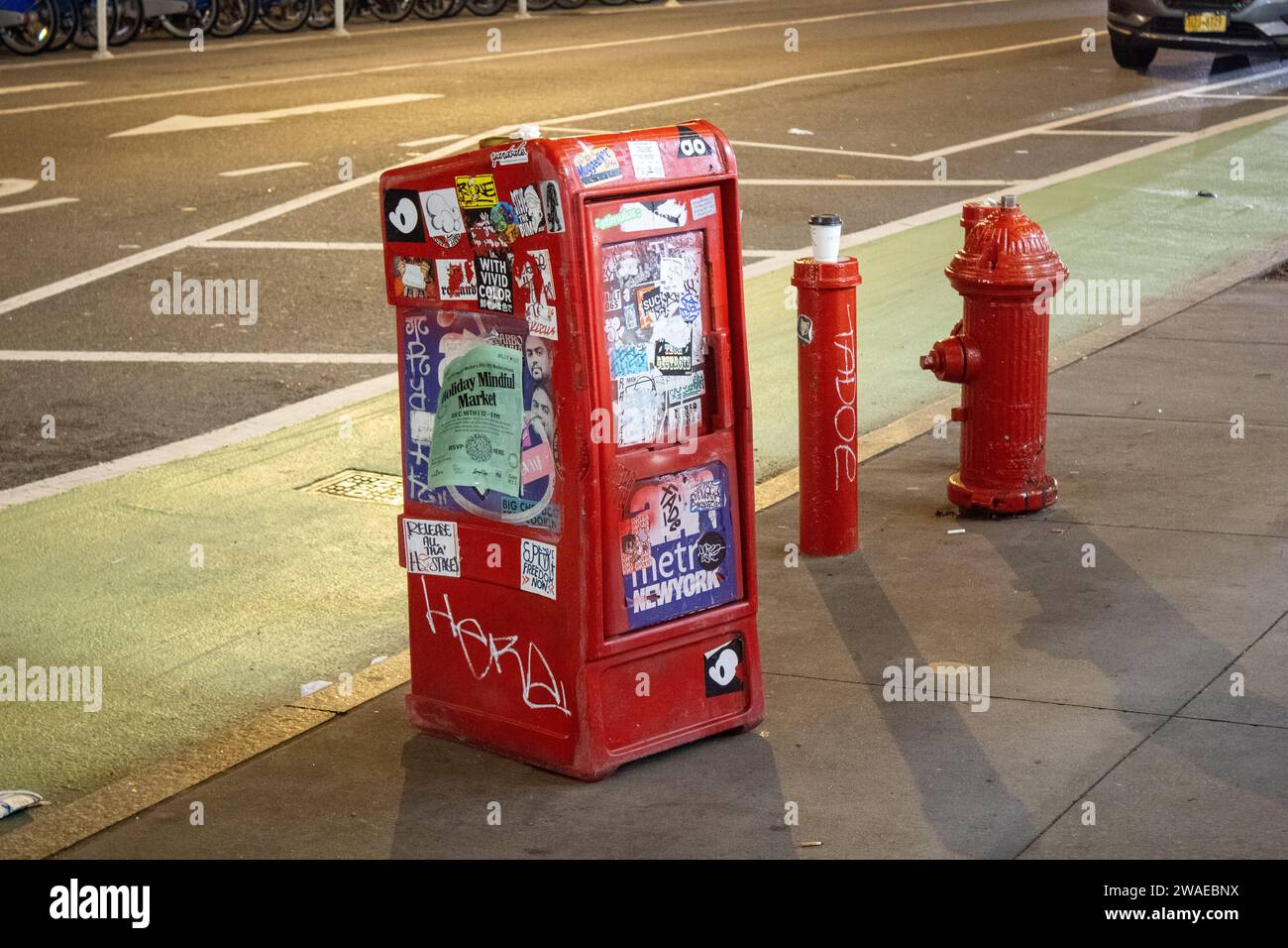 A red newspaper vending machine and a fire hydrant on a city street in ...