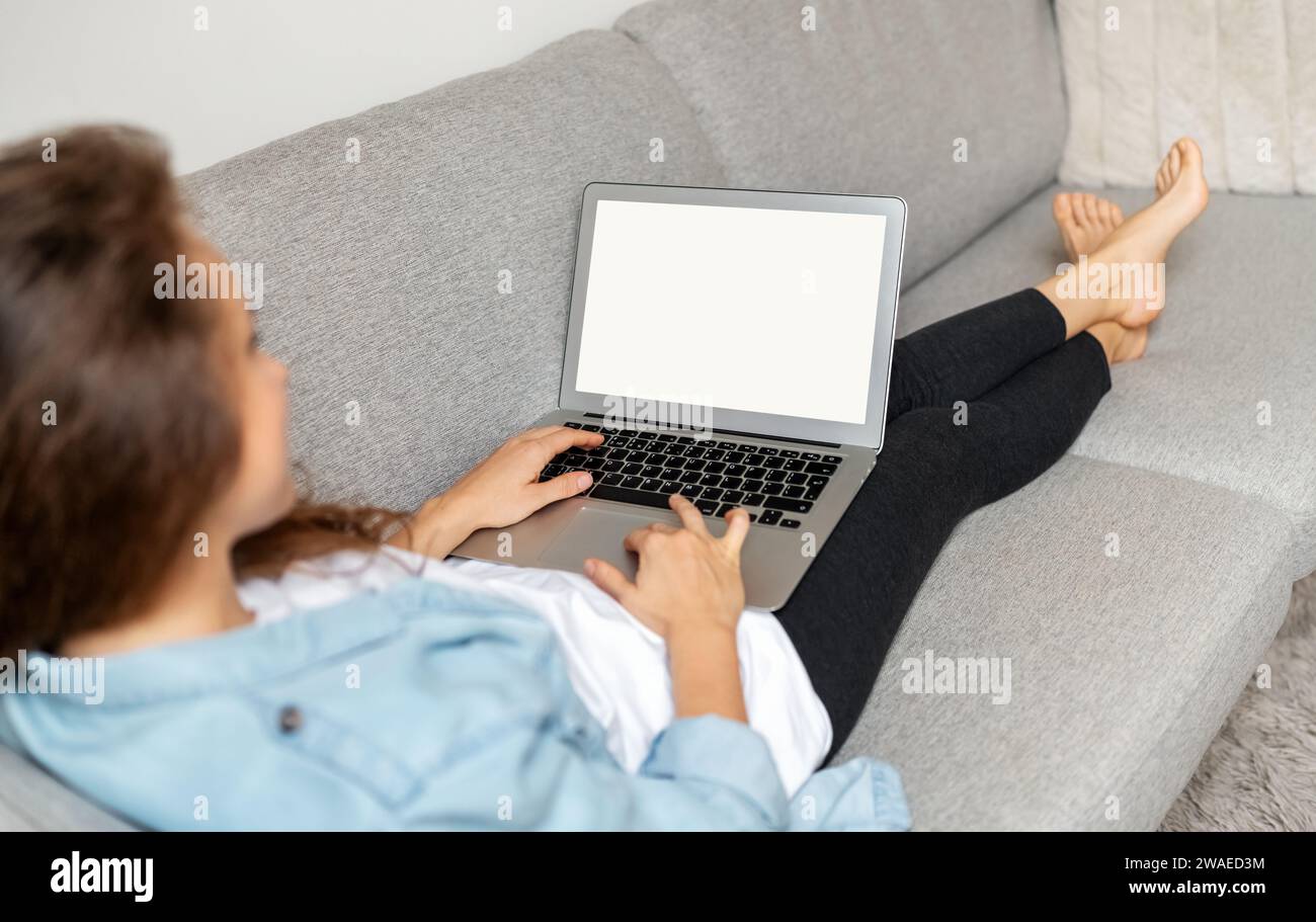 Over the shoulder view laptop with blank screen on laps of woman. Woman ...