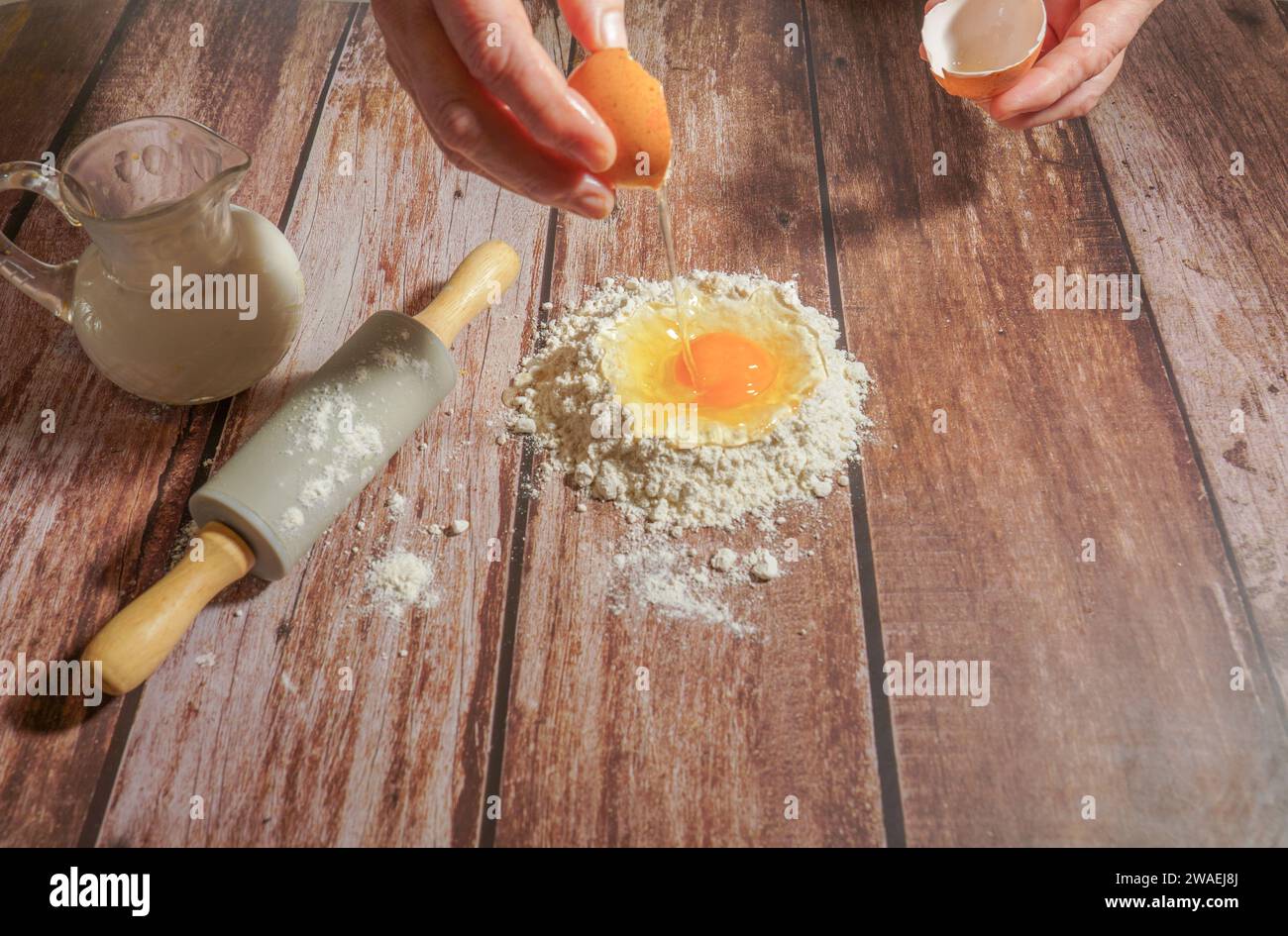 woman breaking an egg, pouring it over flour to make a sponge cake on a ...