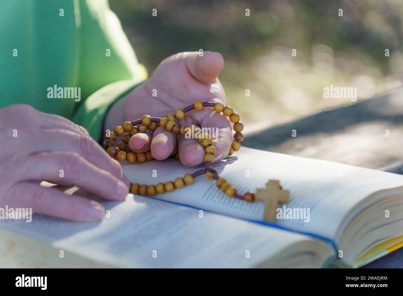 a woman's hands praying the rosary in the field over an open bible on a ...