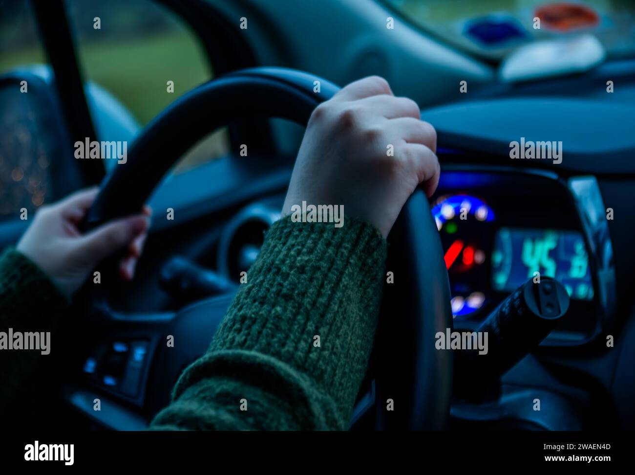 A female driving a modern vehicle in a nighttime setting, hands firmly ...