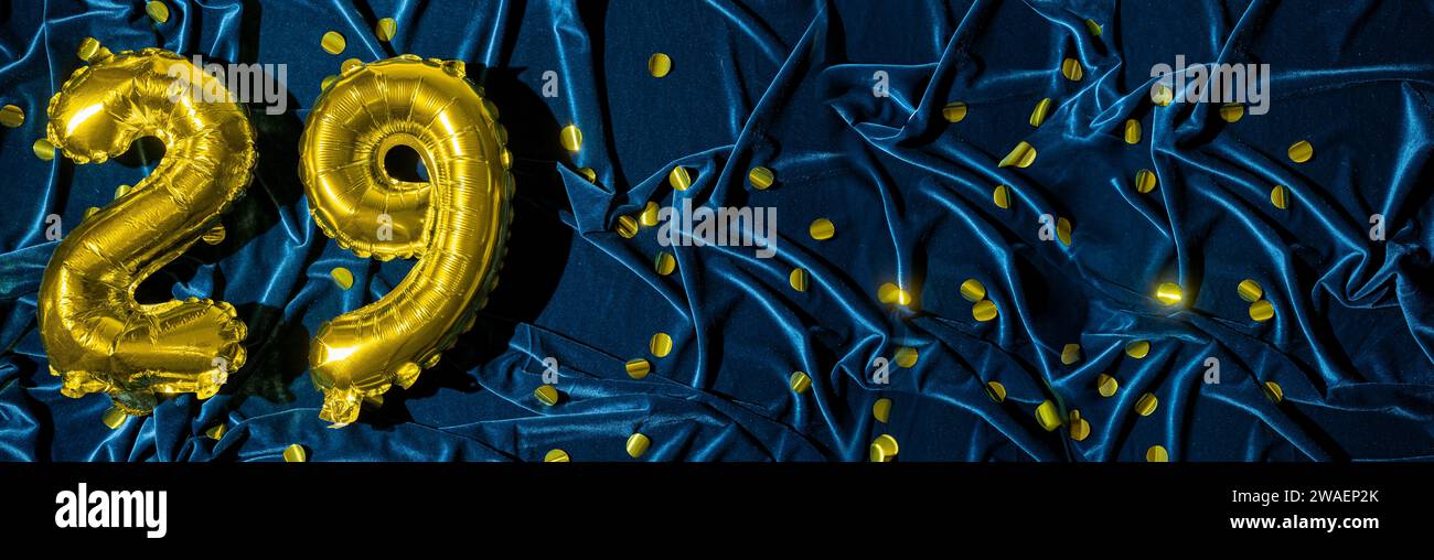 number twenty nine, gold foil balloon number on blue velvet background with confetti. Birthday ...