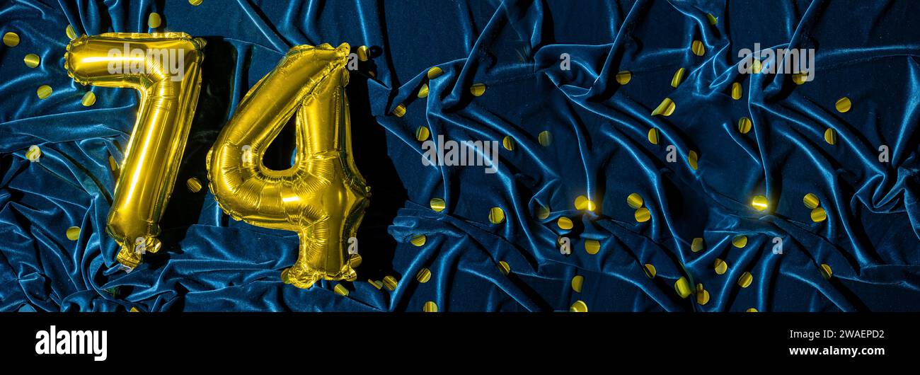 Gold foil balloon number number 74 on a background of blue velvet ...