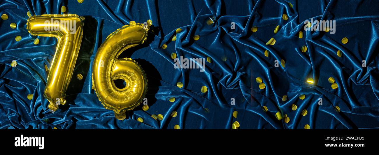 Gold foil balloon number number 76 on a background of blue velvet ...