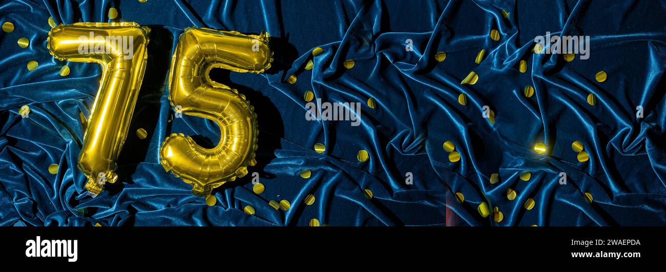 Gold foil balloon number number 75 on a background of blue velvet ...