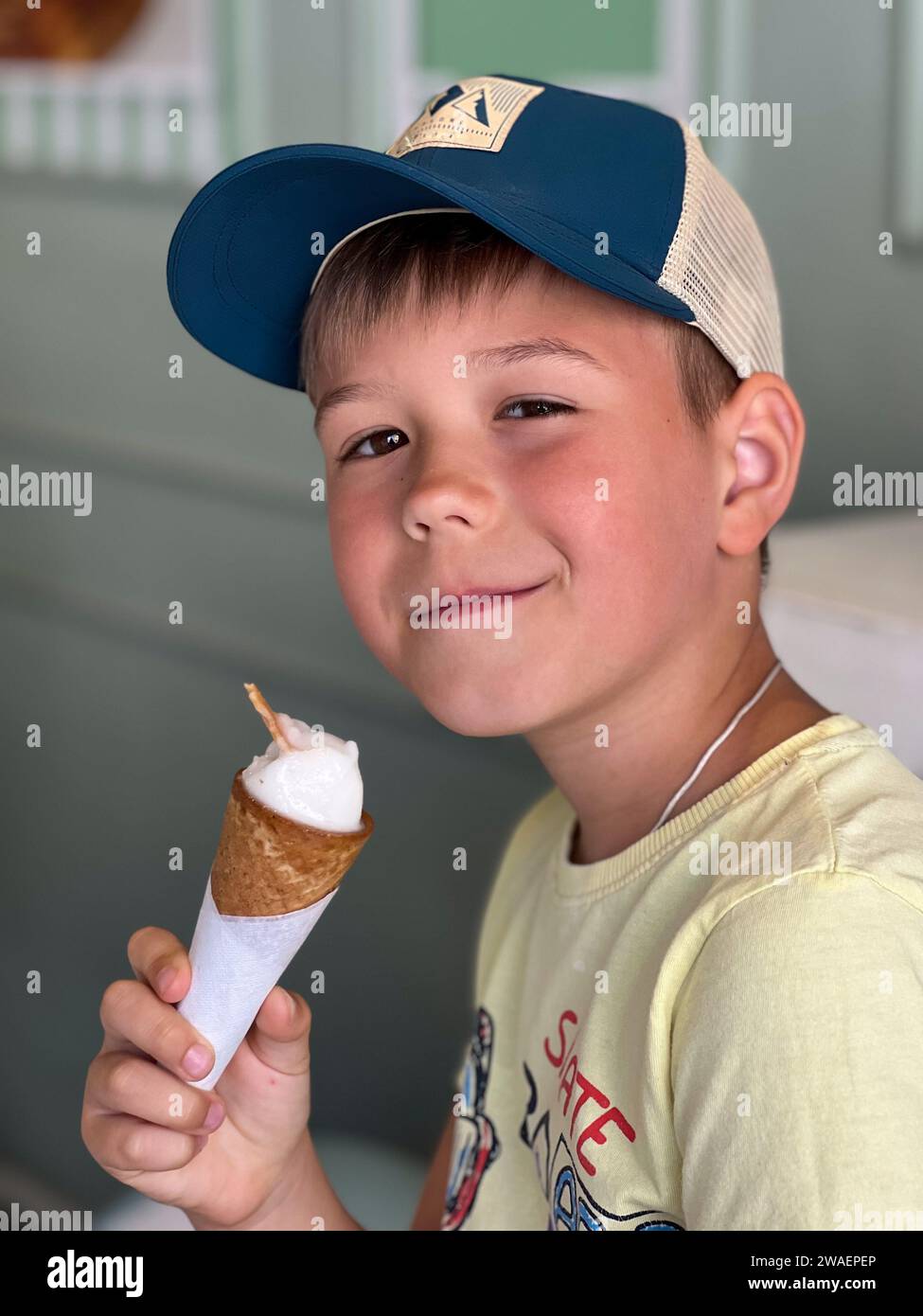 A boy in a yellow T-shirt and cap eats ice cream in a waffle cone Stock ...