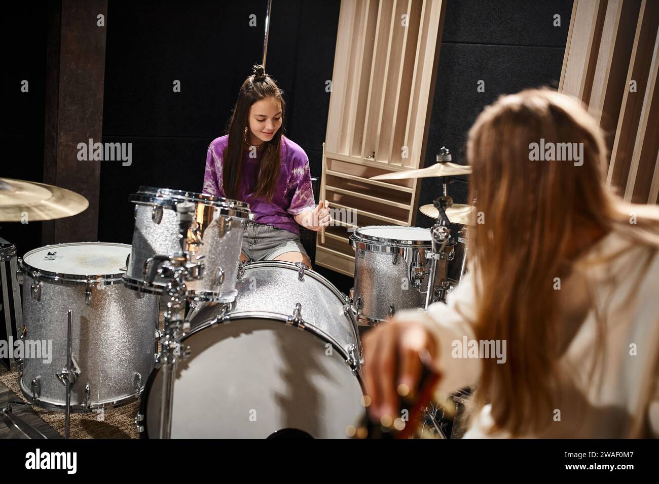 jolly adorable teenage girl playing drums while her blonde friend ...
