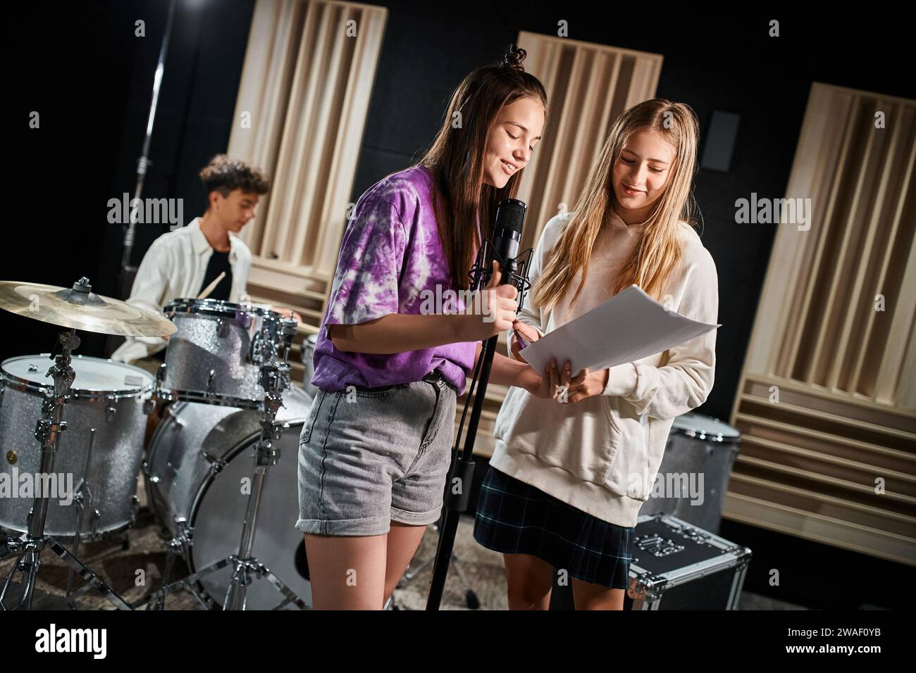 cheerful teenage girls singing into microphone with their friend plying ...
