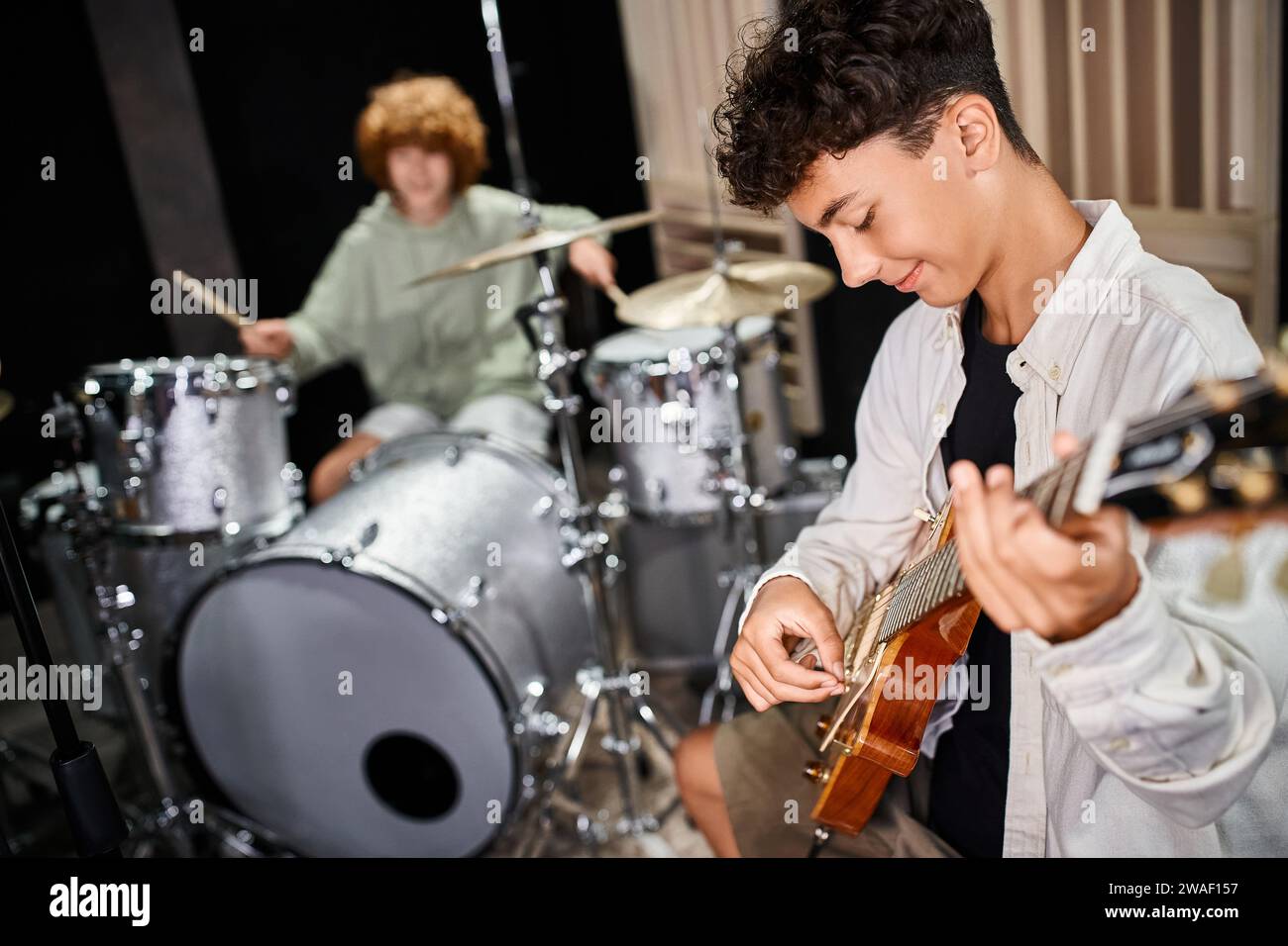 focus on talented adorable teenage boy playing guitar actively next to ...