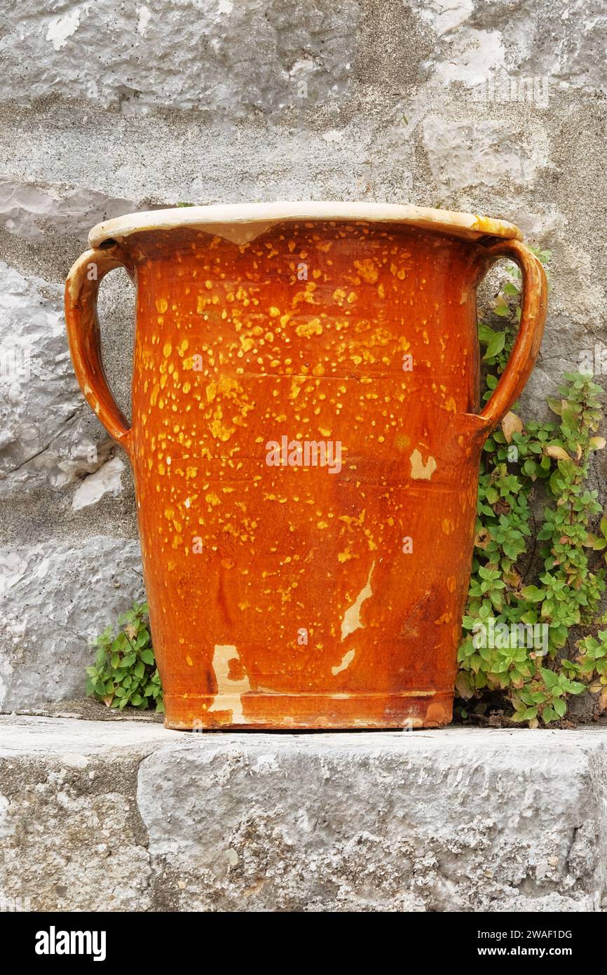 Orange antique ceramic vase stands against a stone wall. Vertical view ...