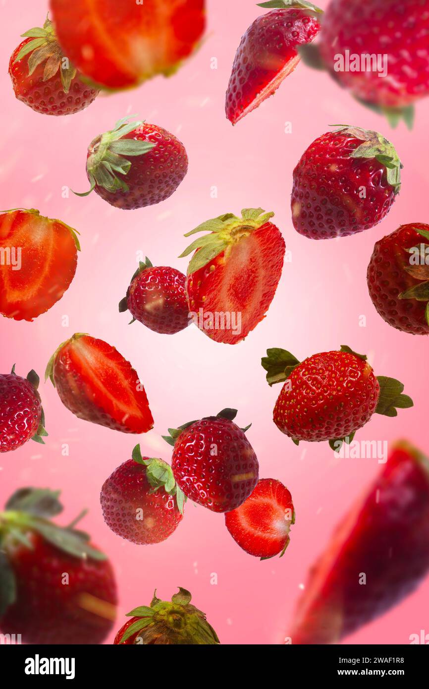 Strawberries and sliced strawberry flying in the air, isolated on pink ...