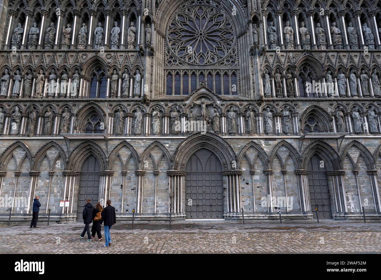 Two people walk near the main facade of the Nidaros Cathedral, located ...