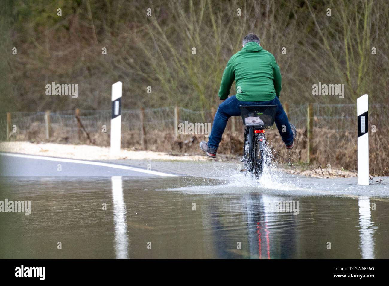 Ebing, Germany. 04th Jan, 2024. A man rides his bicycle over a flooded ...
