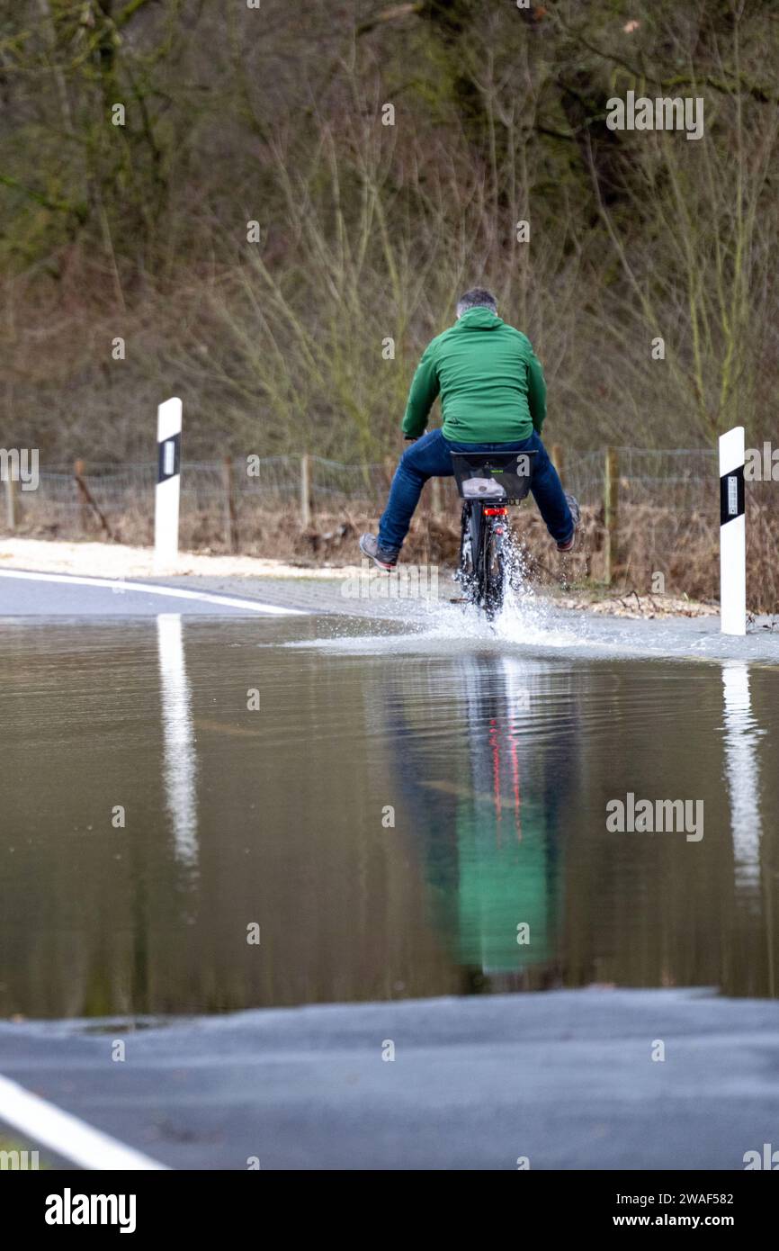 Ebing, Germany. 04th Jan, 2024. A man rides his bicycle over a flooded ...