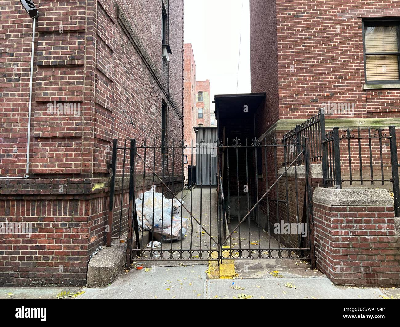 A narrow path with a metal gate between brick buildings Stock Photo - Alamy