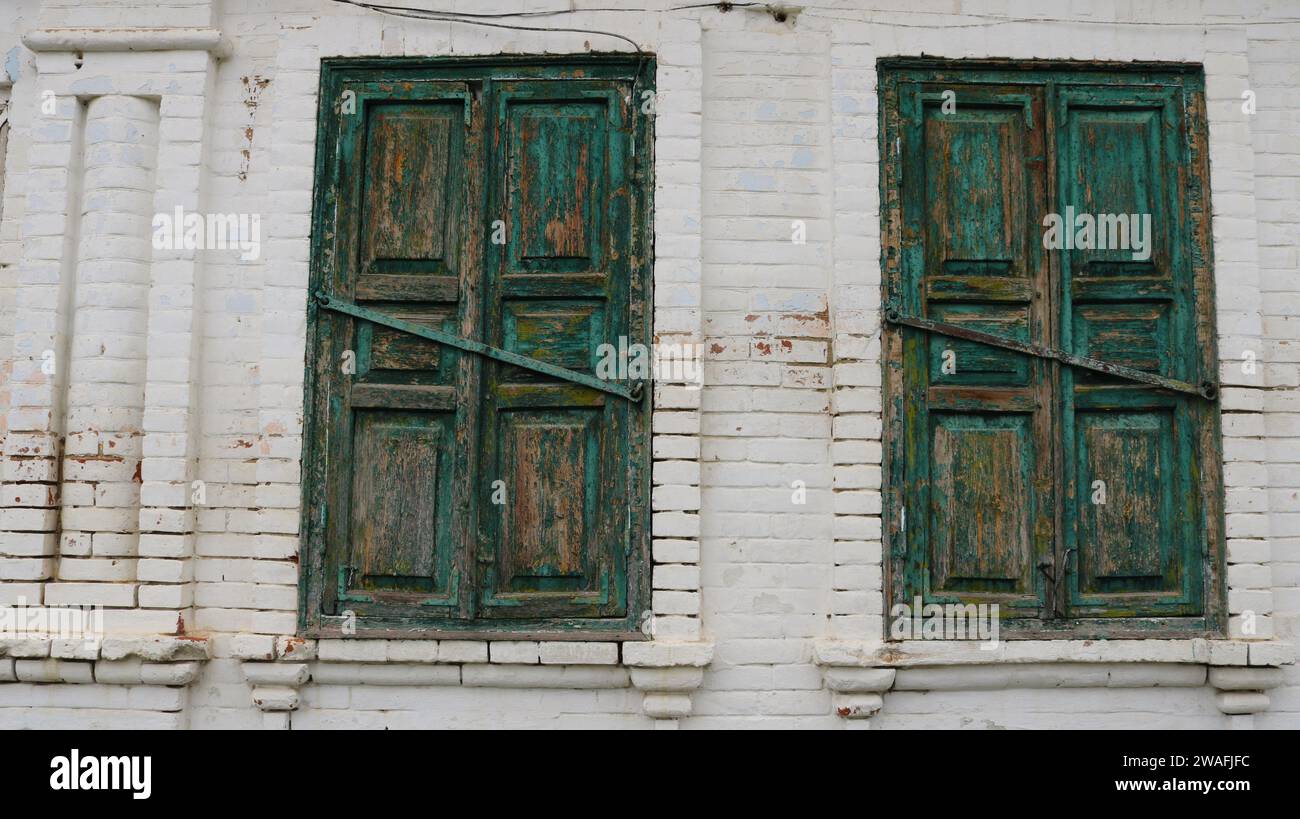 two windows of an old whitewashed house bolted with wooden shutters ...