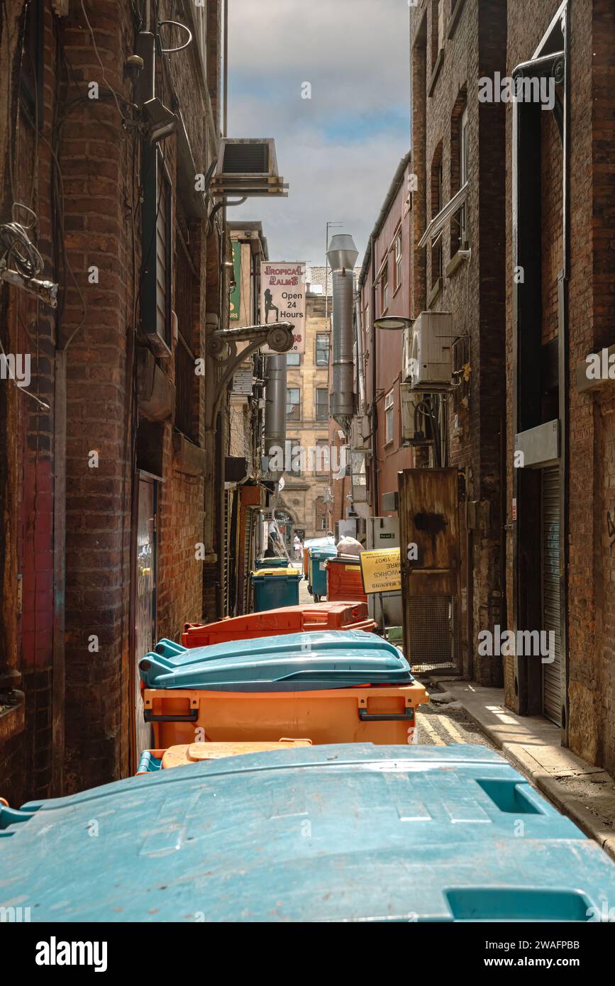 A long narrow alley filled with wheelie bins that pass under a sign for ...