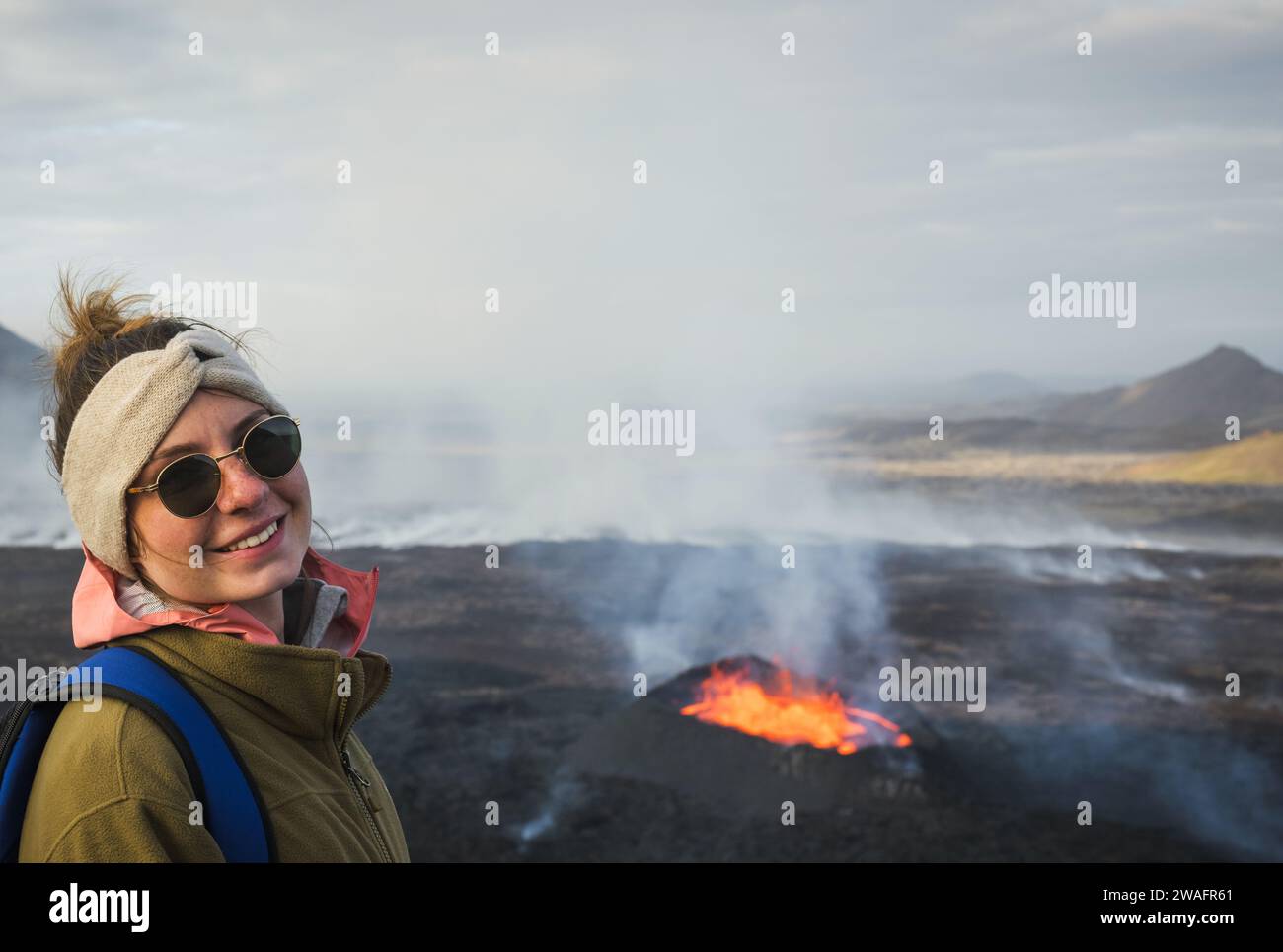 Woman tourist looking at dramatic view of dark volcanic landscape with ...