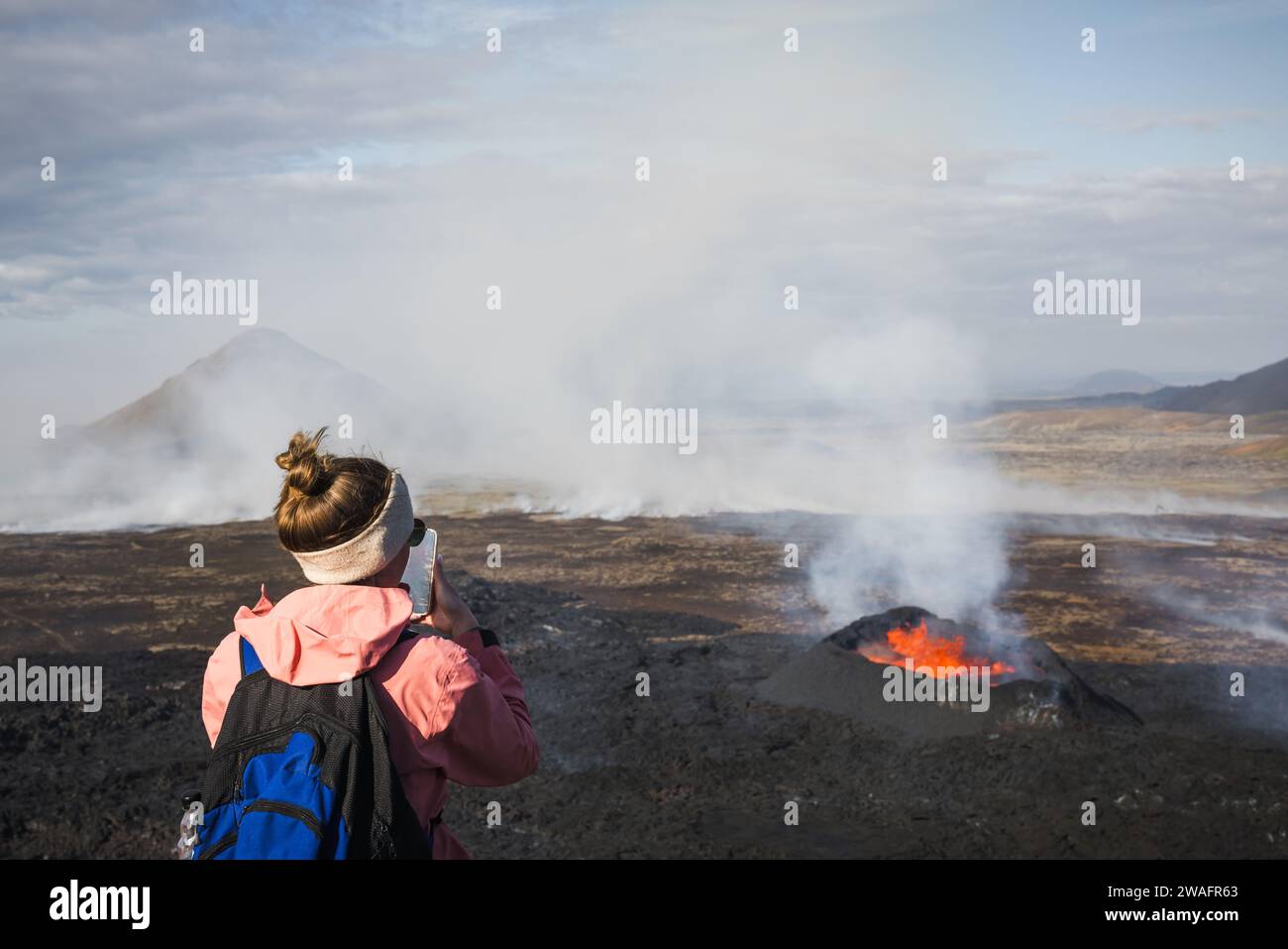 Woman tourist looking at dramatic view of dark volcanic landscape with ...