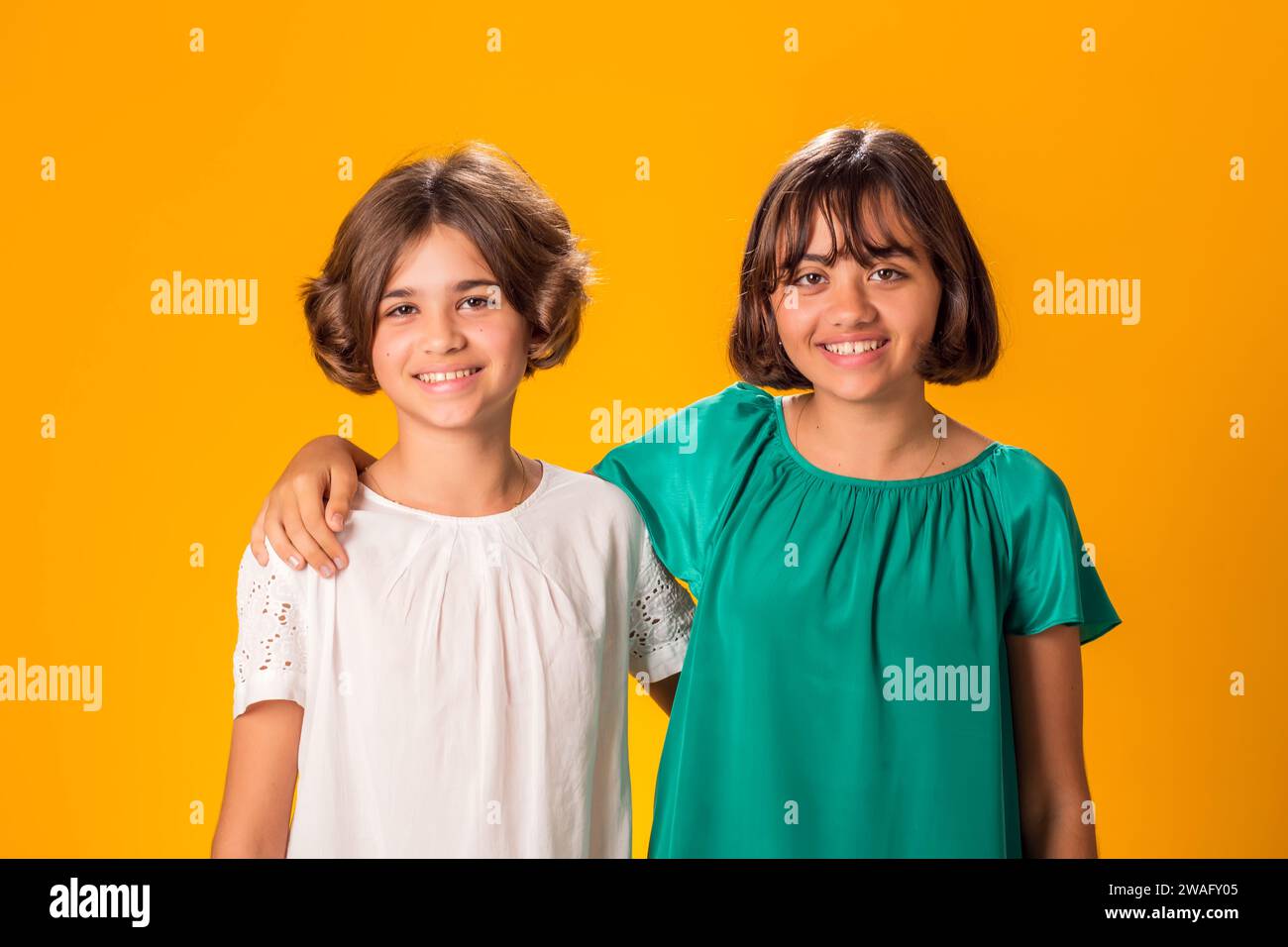 Portrait of two smiling sisters over yellow background. Choldhood and ...