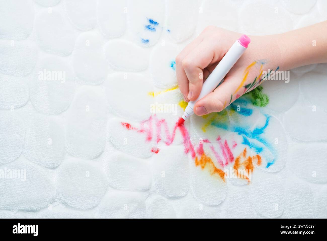 A child's hand drawing felt-tip pens on the white upholstered furniture ...