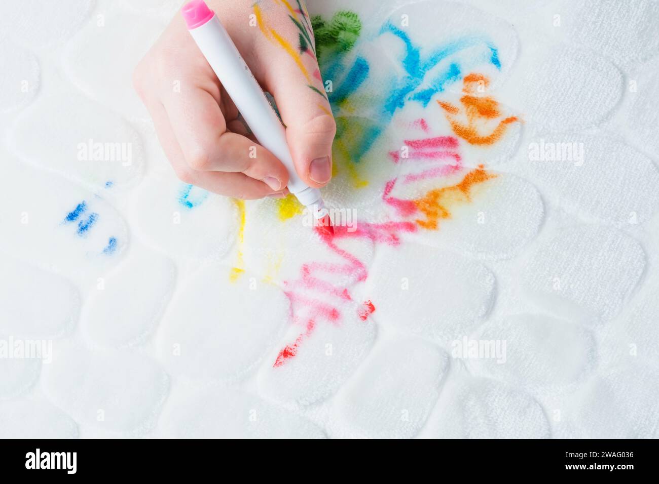 A child's hand drawing felt-tip pens on the white upholstered furniture ...
