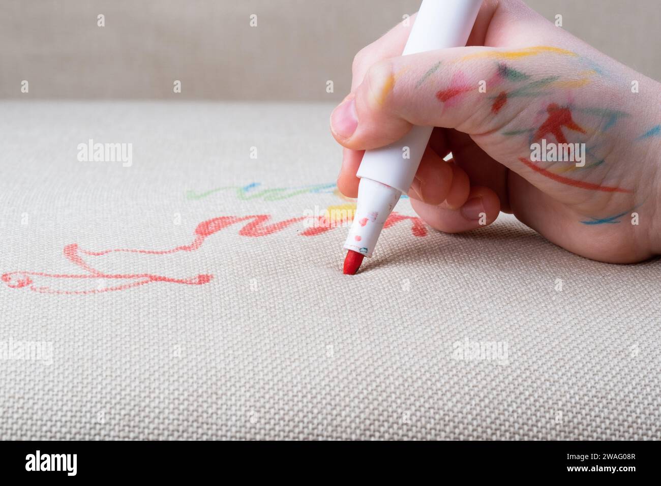 Unrecognizable child drawing felt-tip pens on the sofa or a carpet ...