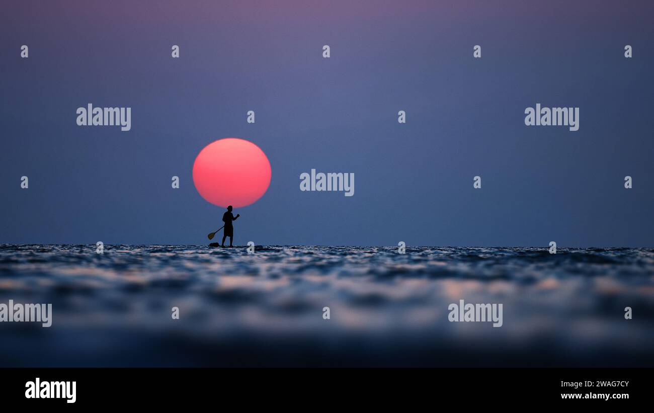 Silhouette of a man on the paddleboard against the setting sun ...
