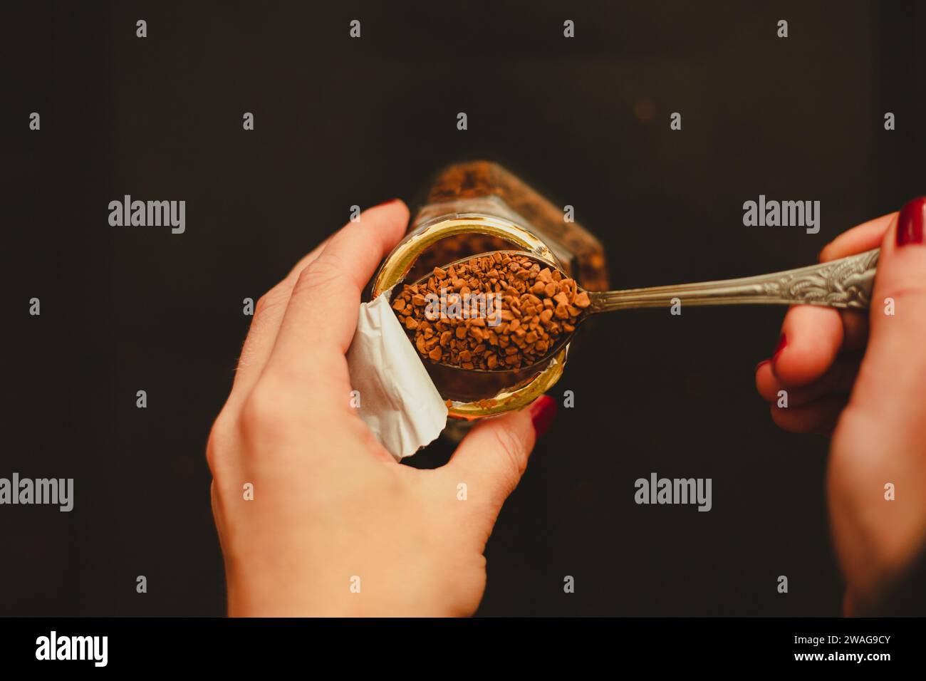 The woman takes out a portion of instant coffee from a jar with a ...