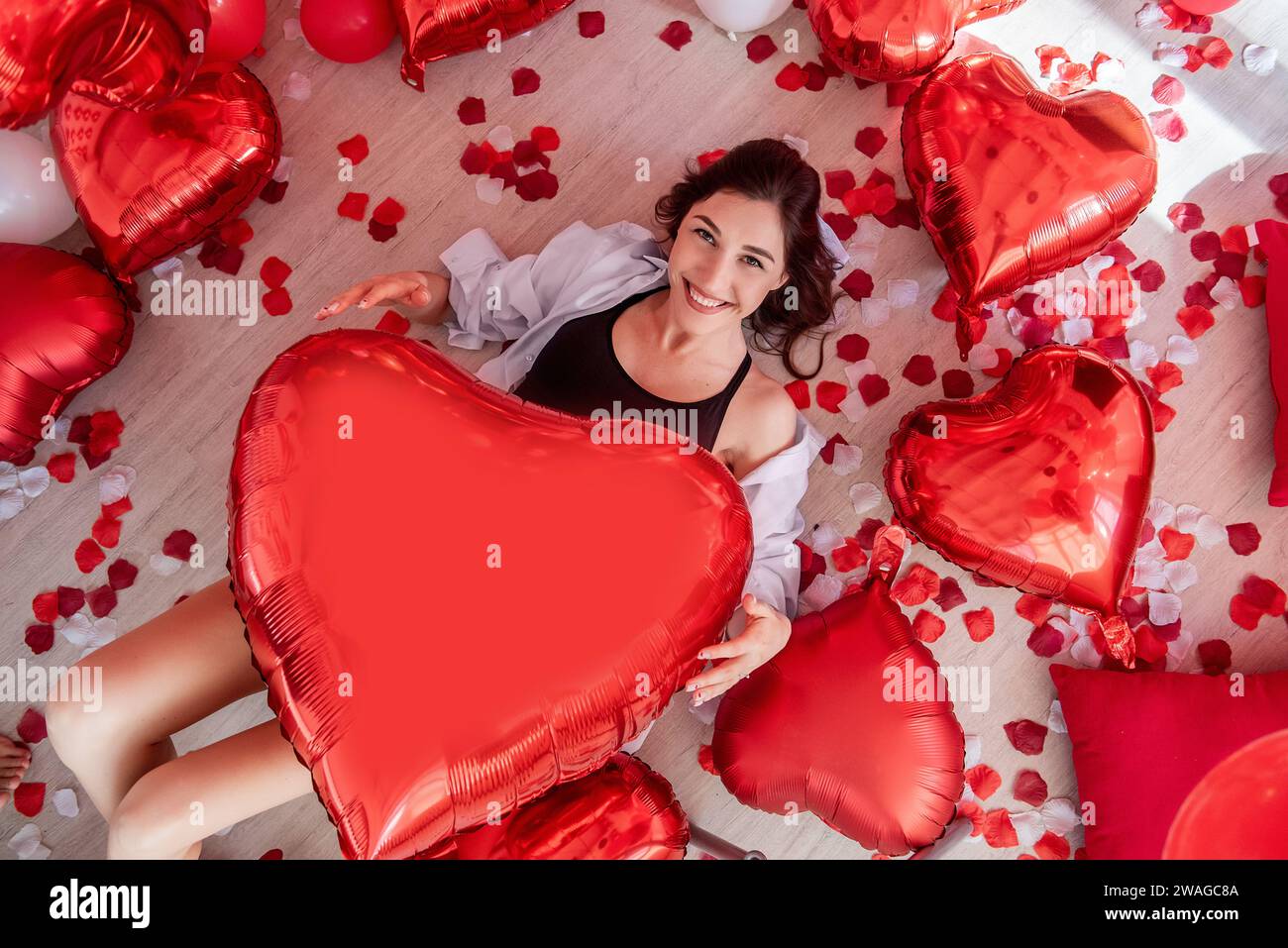 Top view of young woman lying on wooden floor holding a big red heart ...