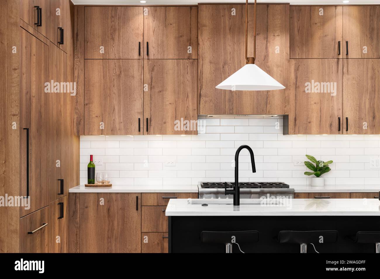 A kitchen detail with wood cabinets, a black faucet, subway tile ...