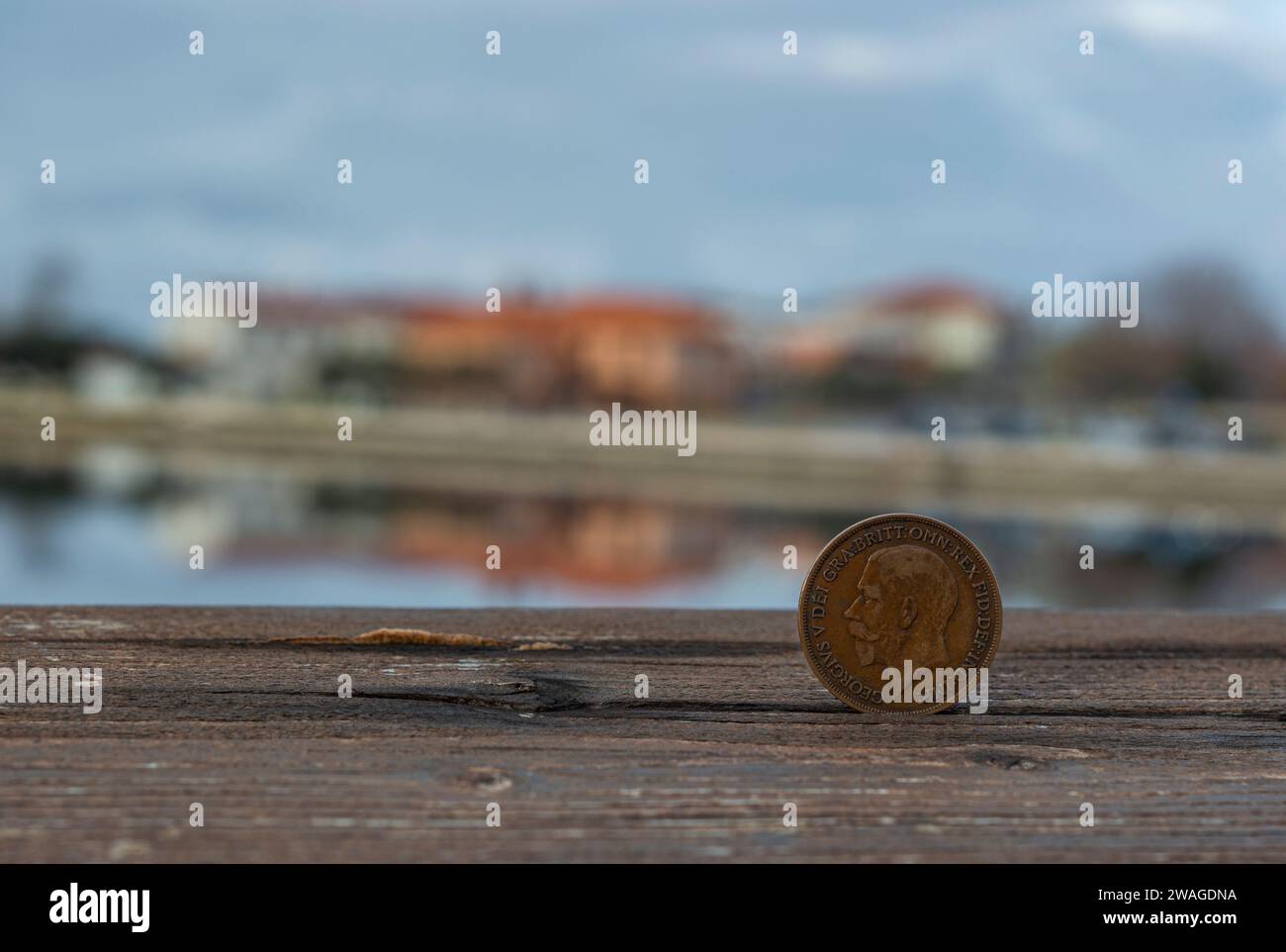 A single penny is placed on a wooden table that overlooks a calm body ...