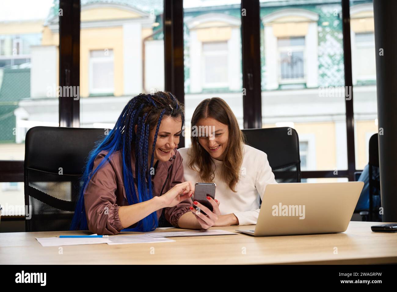 Female friends having fun sitting together in bright coworking office ...