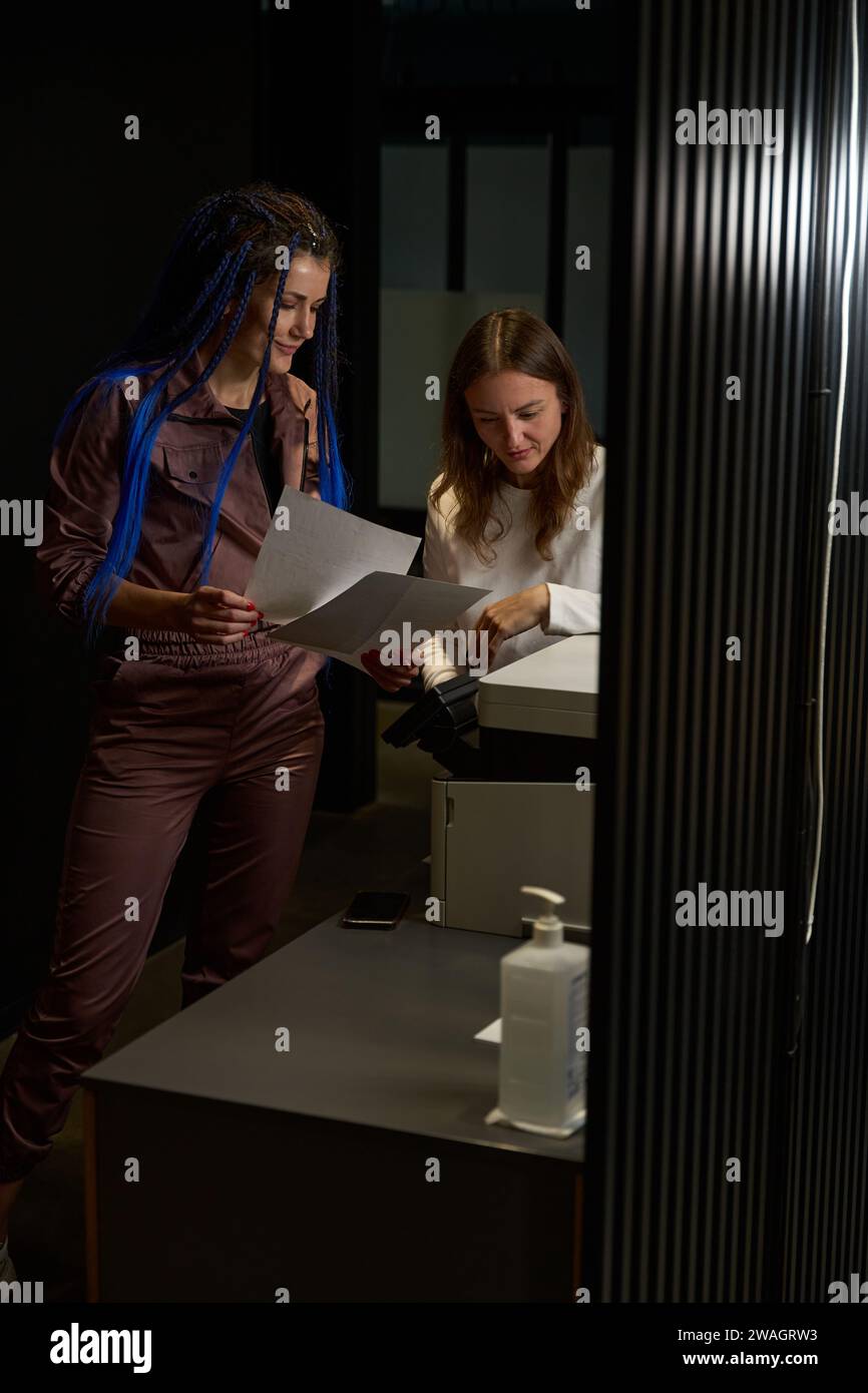 Two women colleagues making copies of documents on copier in copy room ...