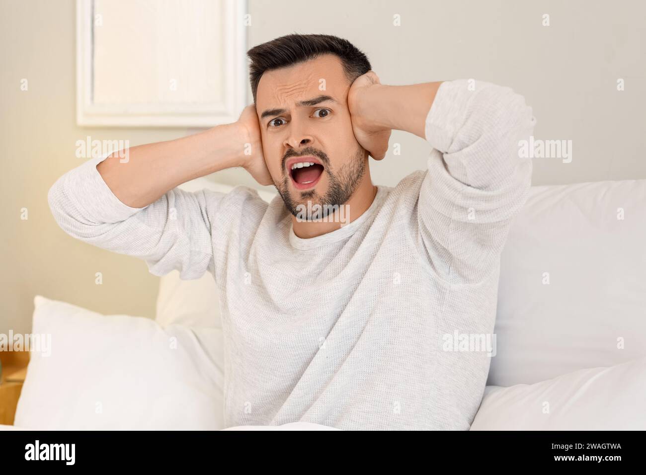 Angry young man suffering from loud neighbours in bedroom Stock Photo ...