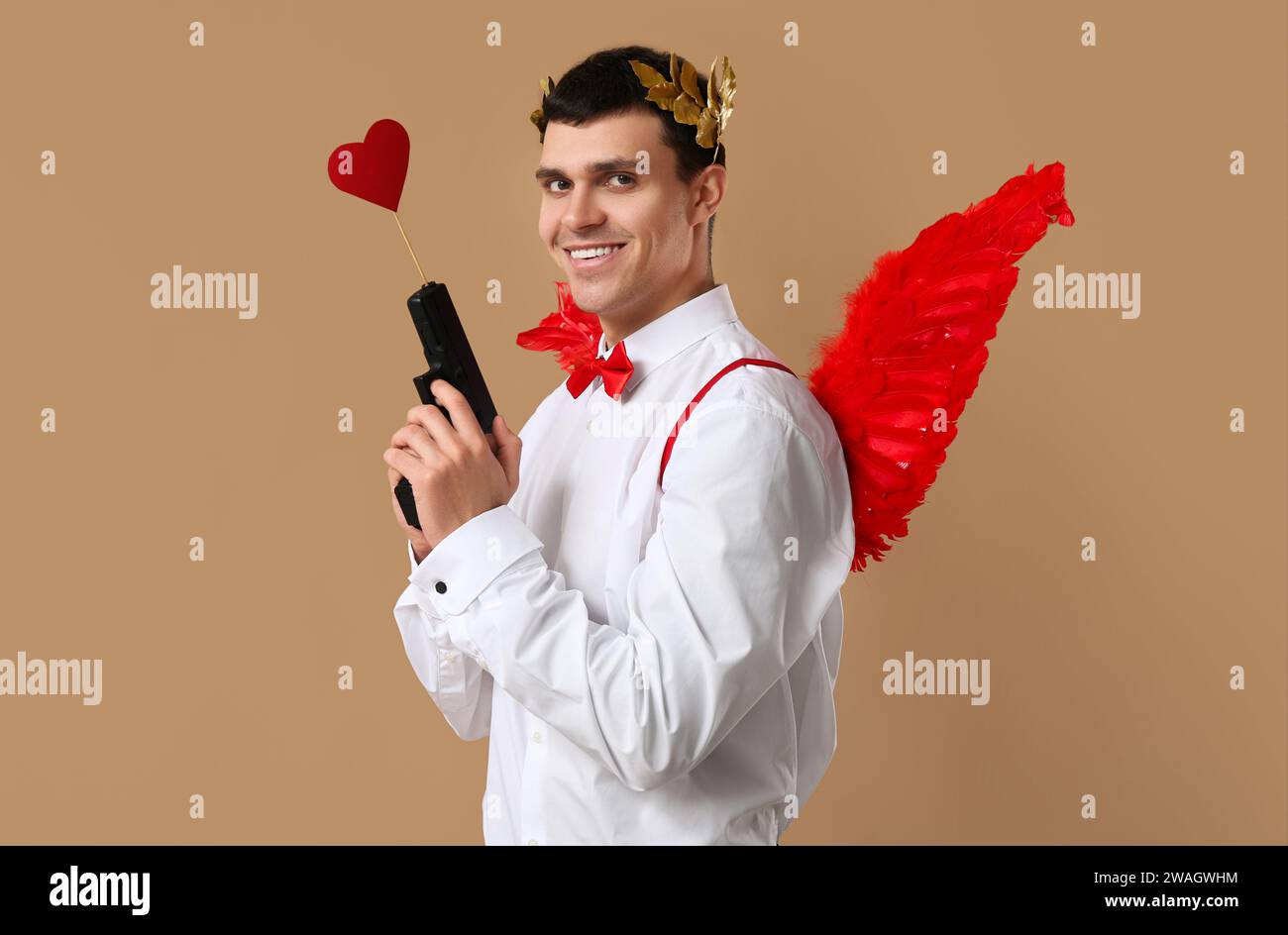 Cool young man dressed as Cupid with gun on beige background. Valentine ...