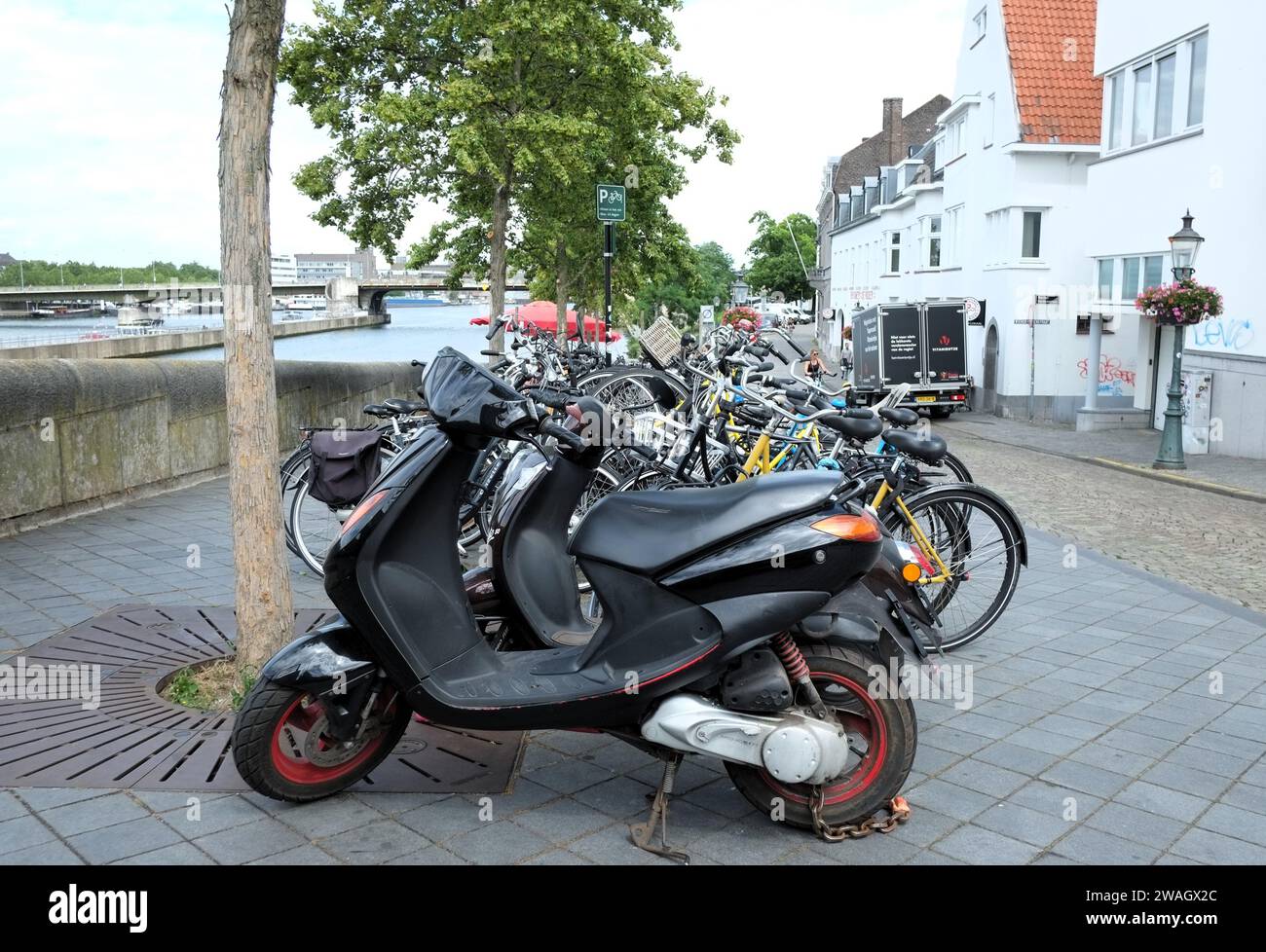 Bicycles and scooters parked on the sidewalk alongside the Maas in ...