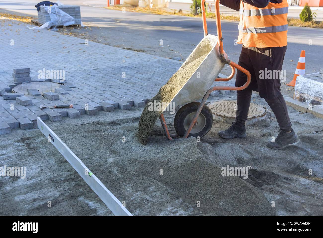 Pouring sand from wheelbarrow onto footpath in preparation for laying ...