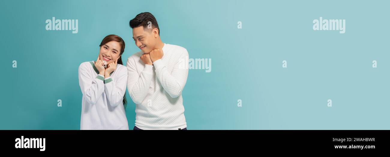 Optimistic young couple keeping hands near cheeks and looking at camera ...